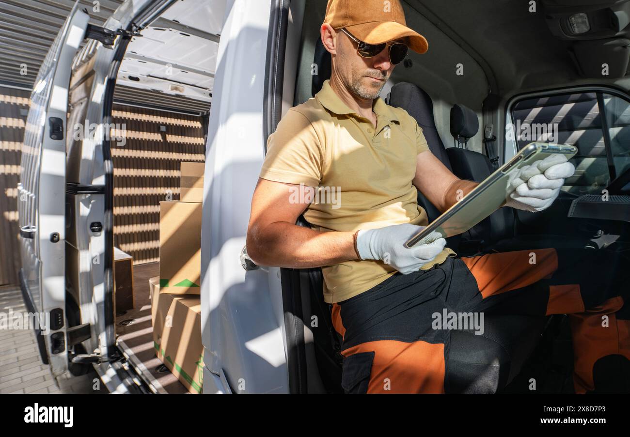 Caucasian courier seating inside delivery van and performing parcel ...
