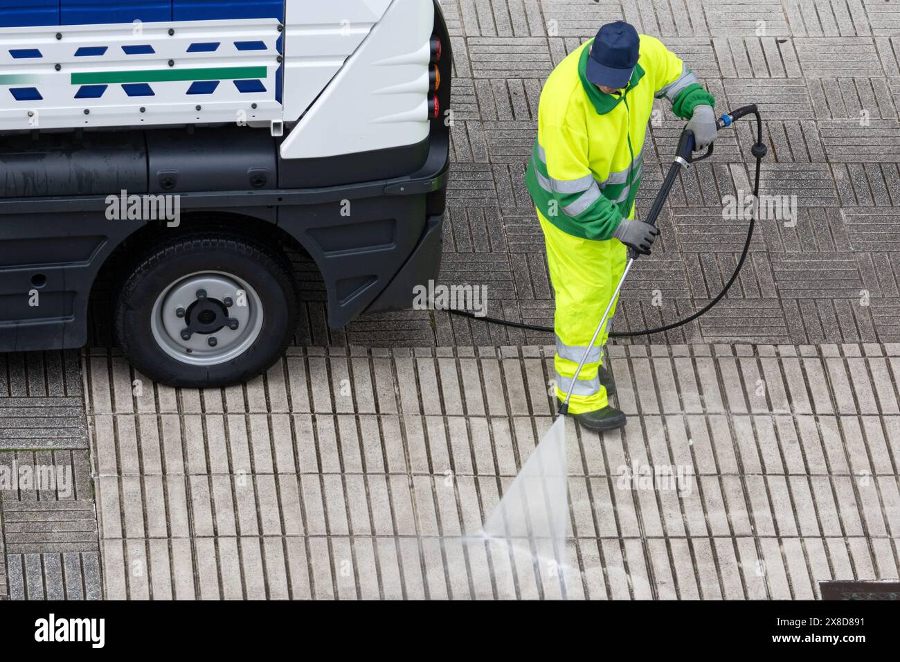 Worker cleaning a street sidewalk with high pressure water jet machine ...