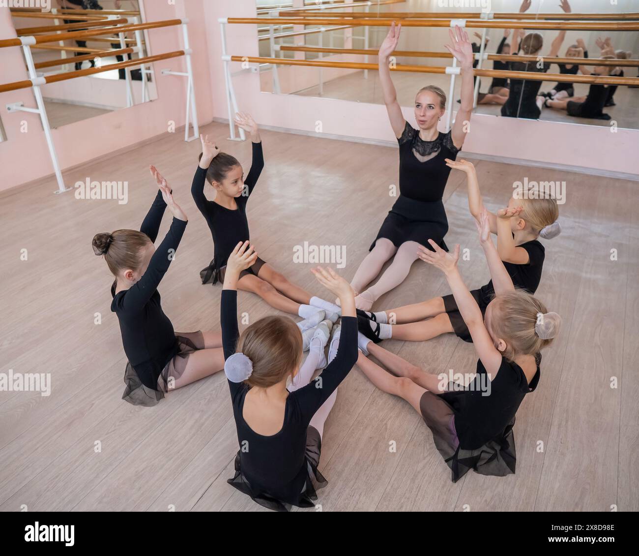 Caucasian woman and five little girls sit in a circle and do stretching ...