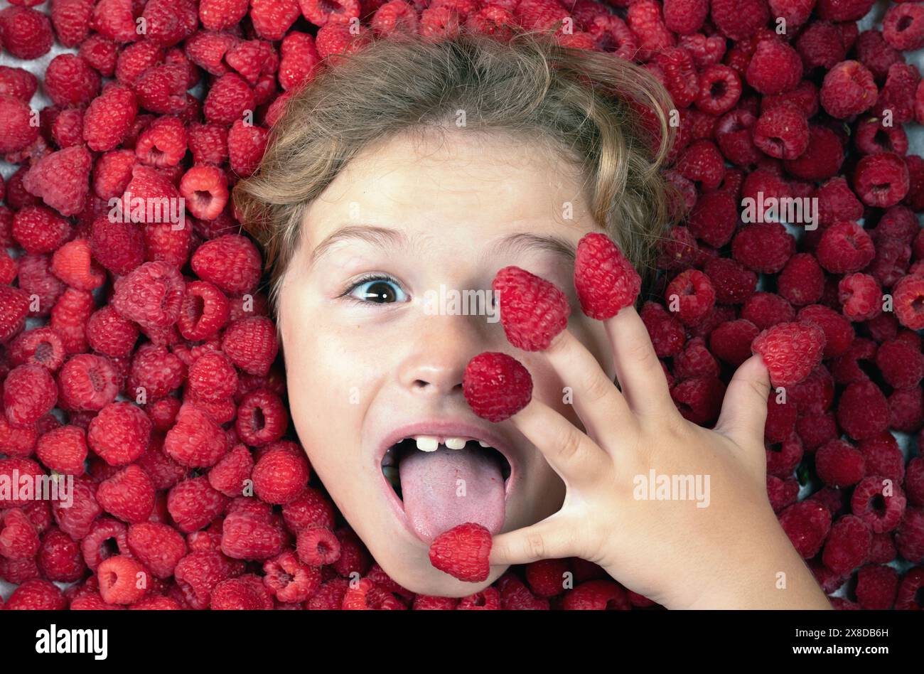 Excited child face with raspberries. Raspberries child face close up ...