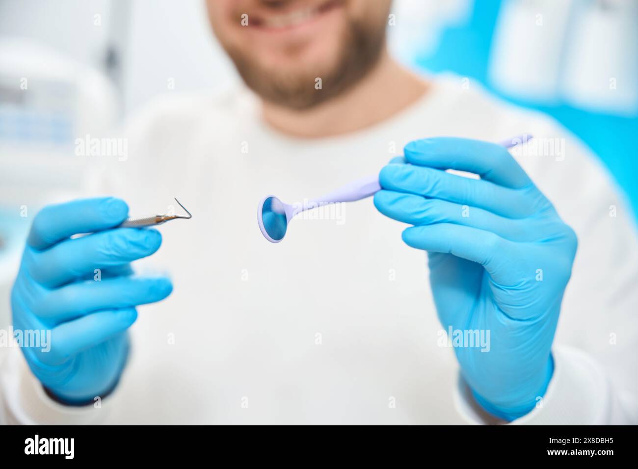 Smiling bearded dentist holding sterile mouth mirror and sickle probe ...