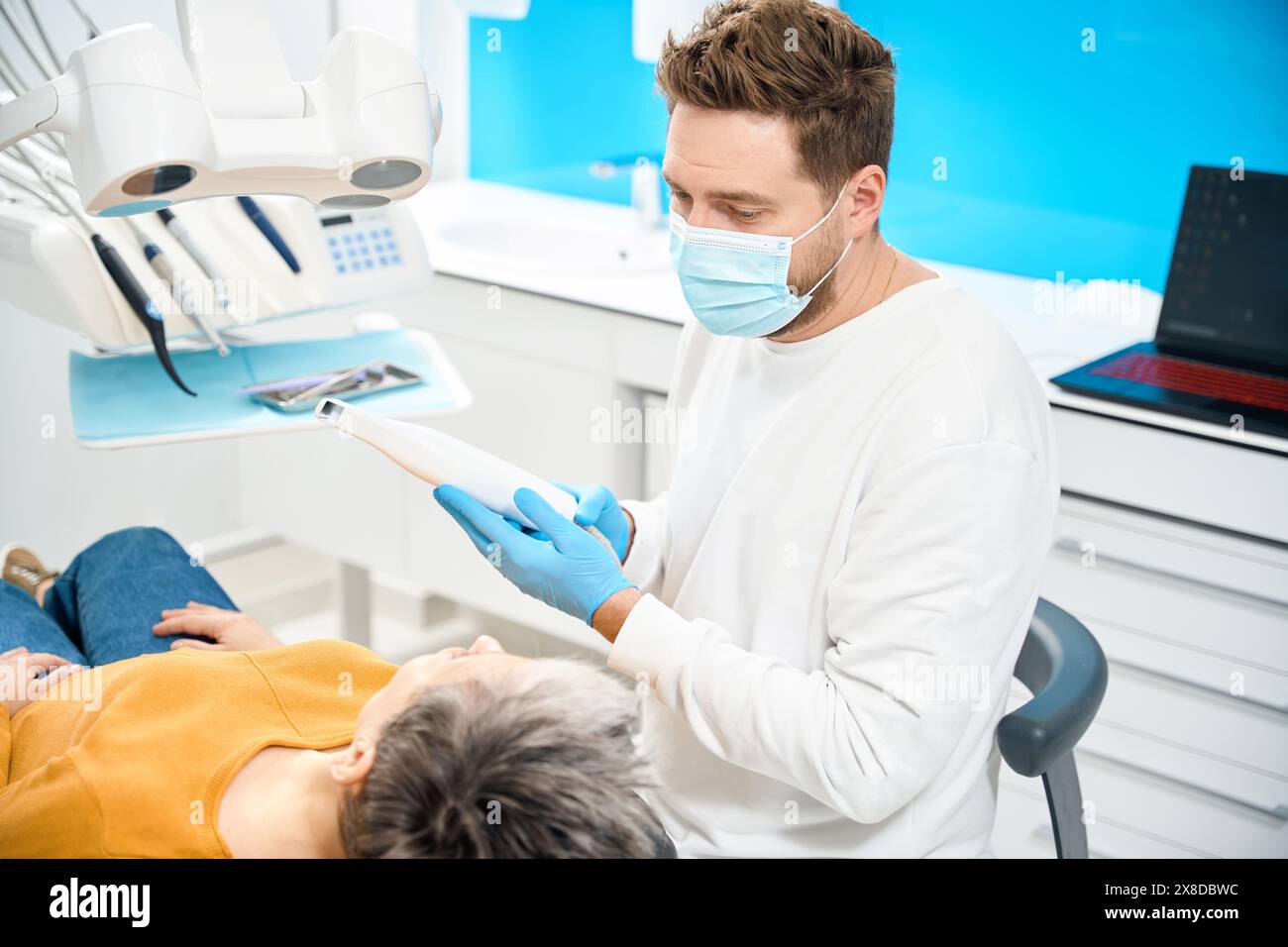 Dental practitioner showing portable dental scanner to woman patient ...
