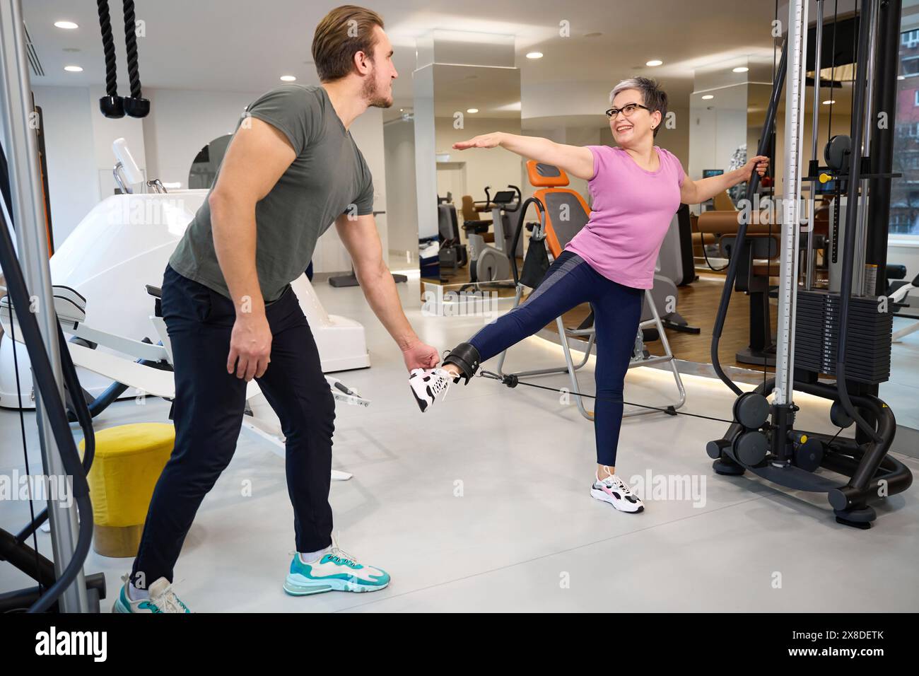 Male trainer helping smiling adult caucasian woman doing sport exercise ...