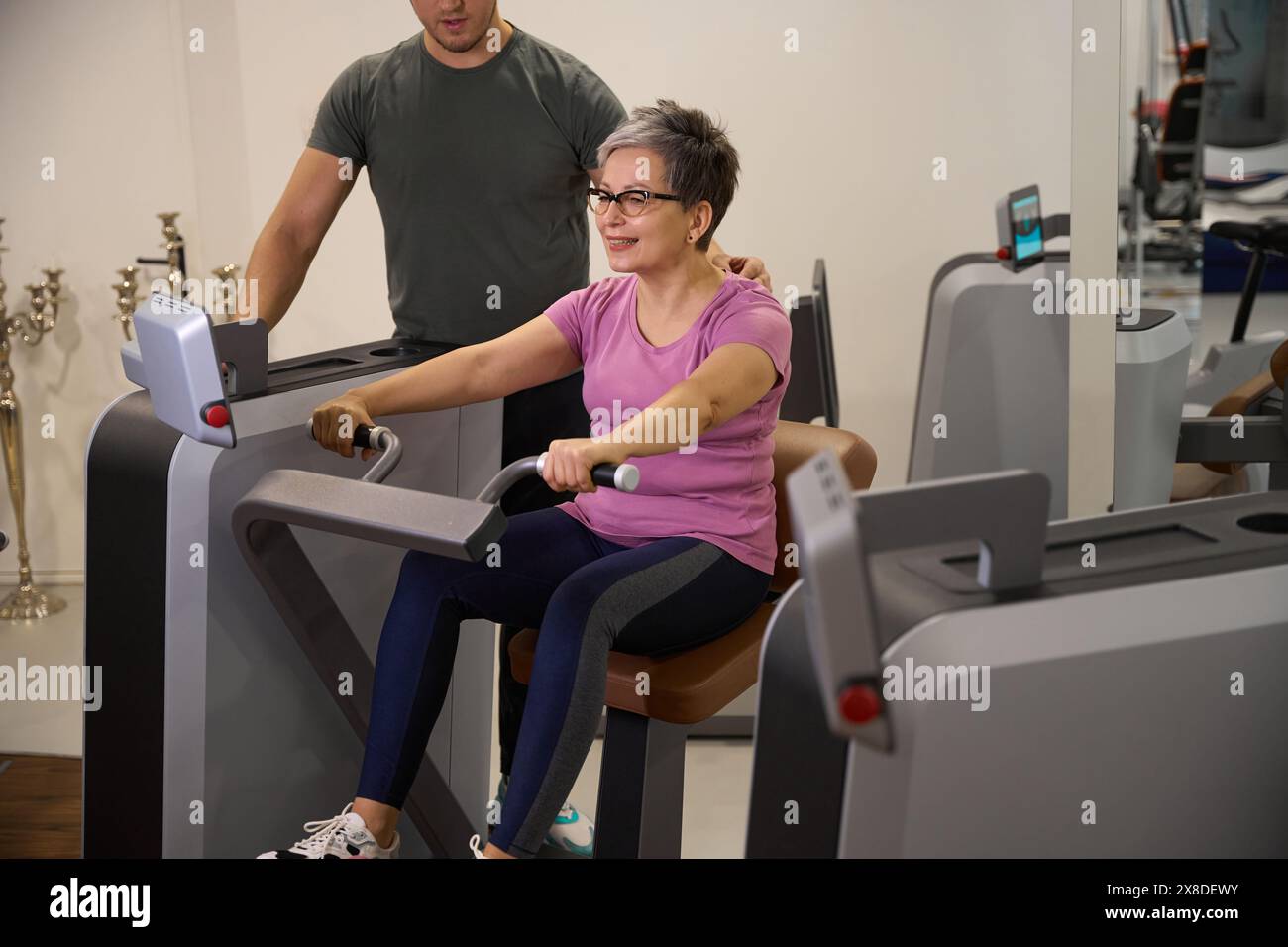 Trainer teaching mature woman doing sport exercise for legs on sport ...