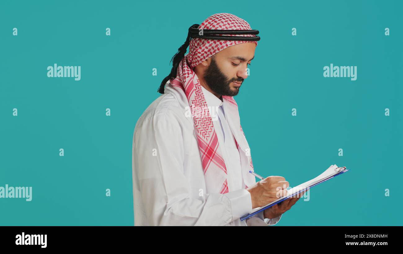Arab man writing letter on papers standing over blue background ...