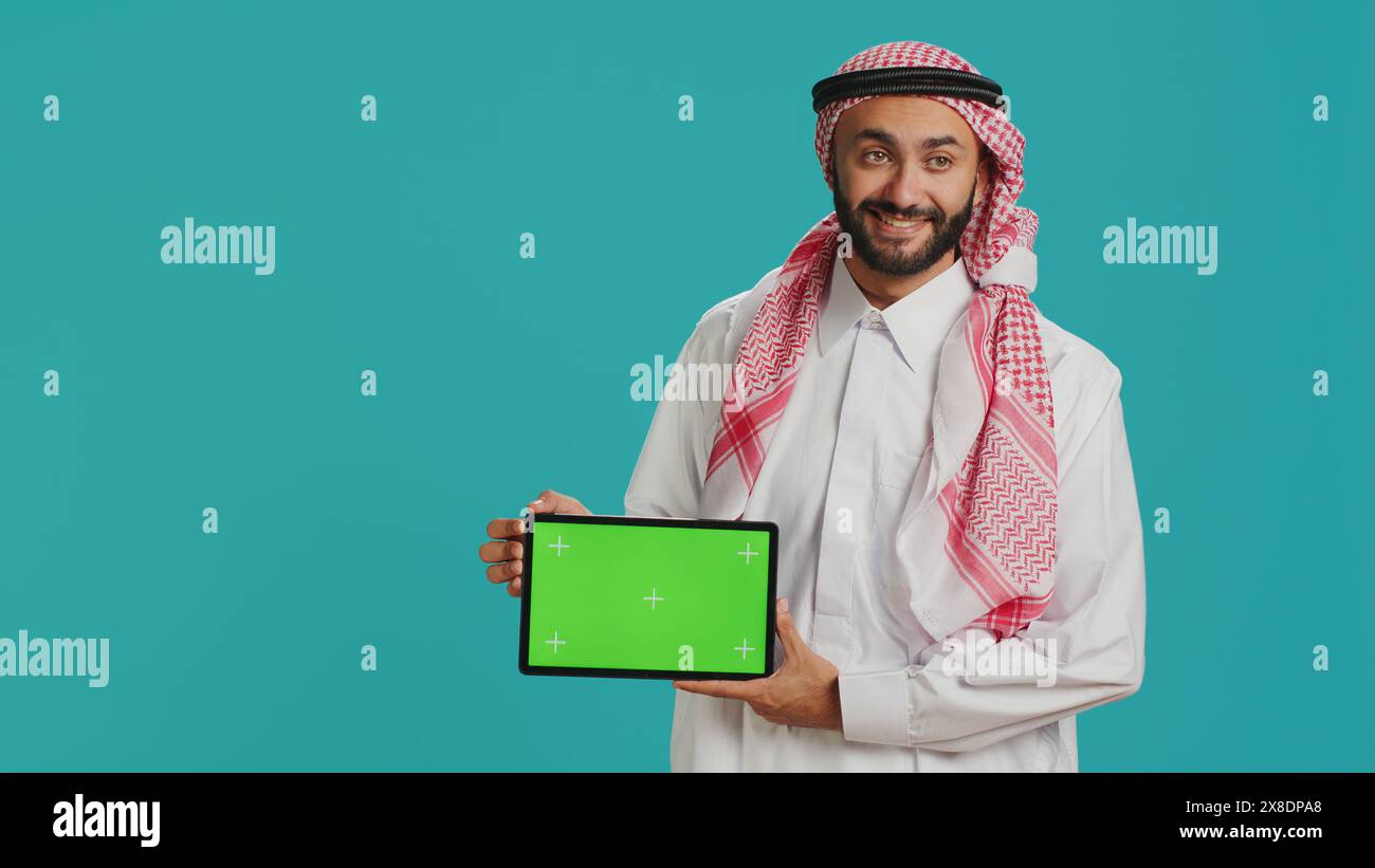 Arab man showing greenscreen on tablet over blue background, presenting ...