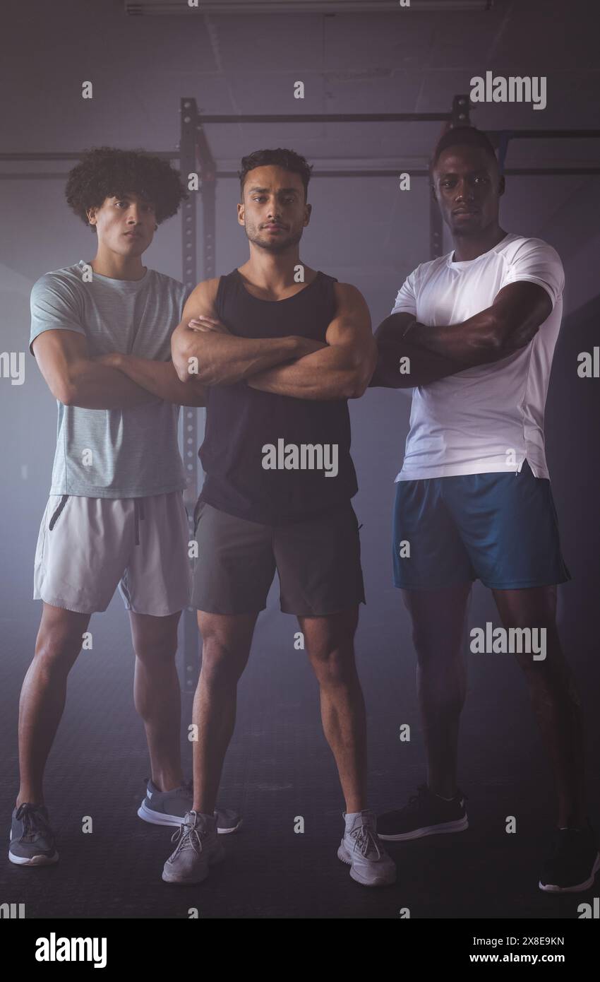 At gym, three young, fit, diverse men standing confidently with arms ...