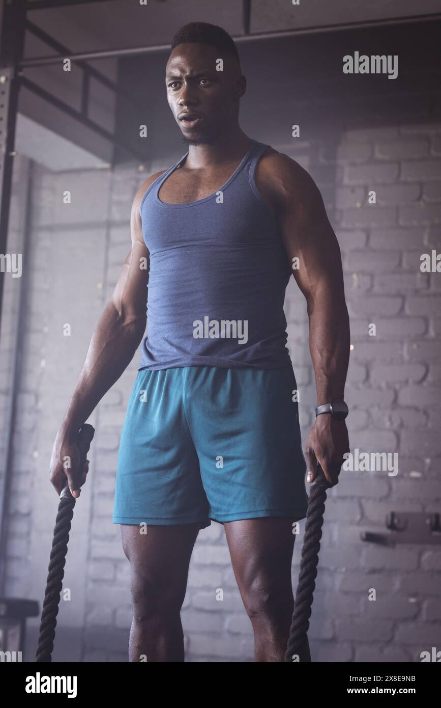 At gym, strong and fit African American man holding battle ropes ...