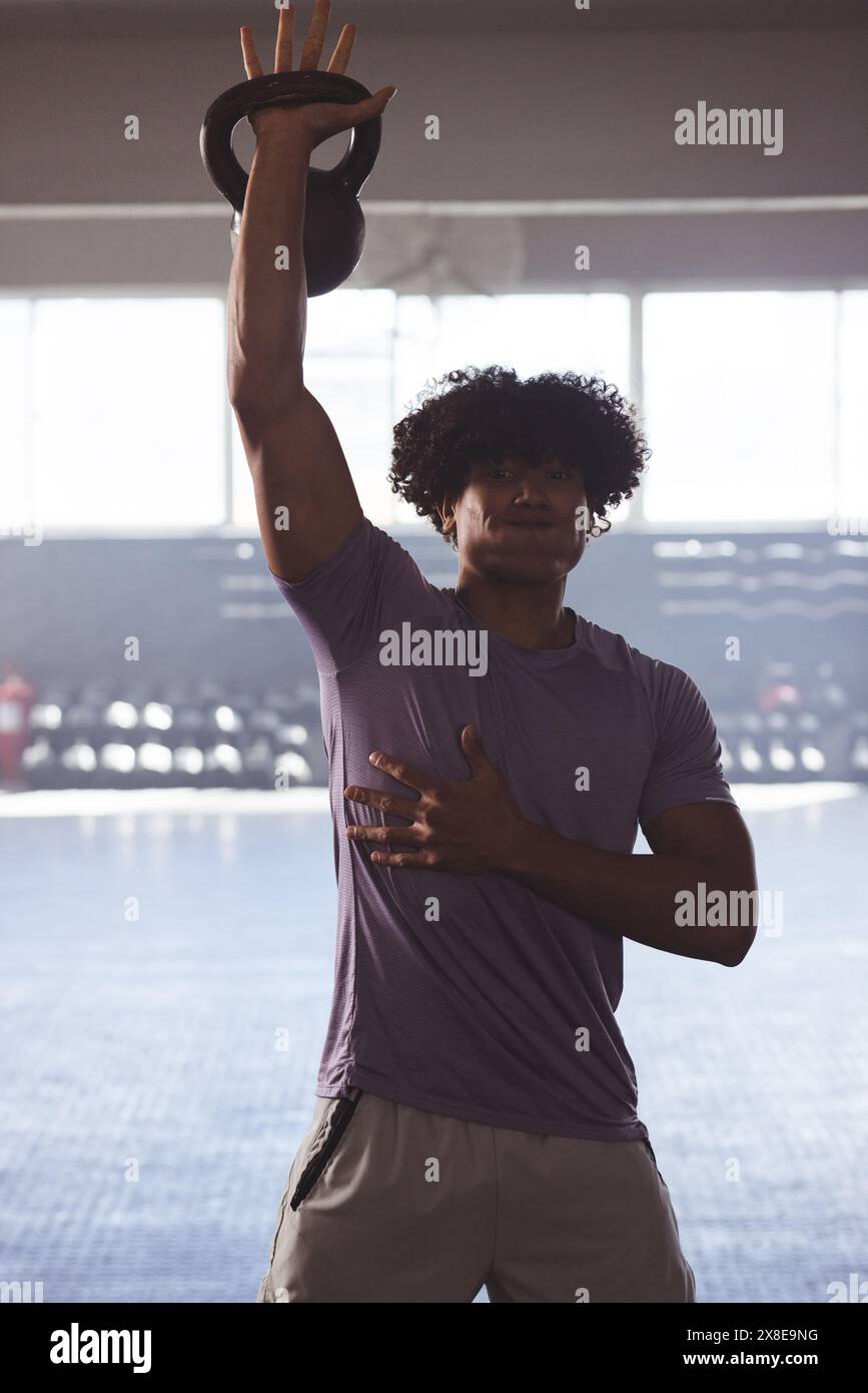 Young biracial man fitness enthusiast at gym lifting kettlebell with ...