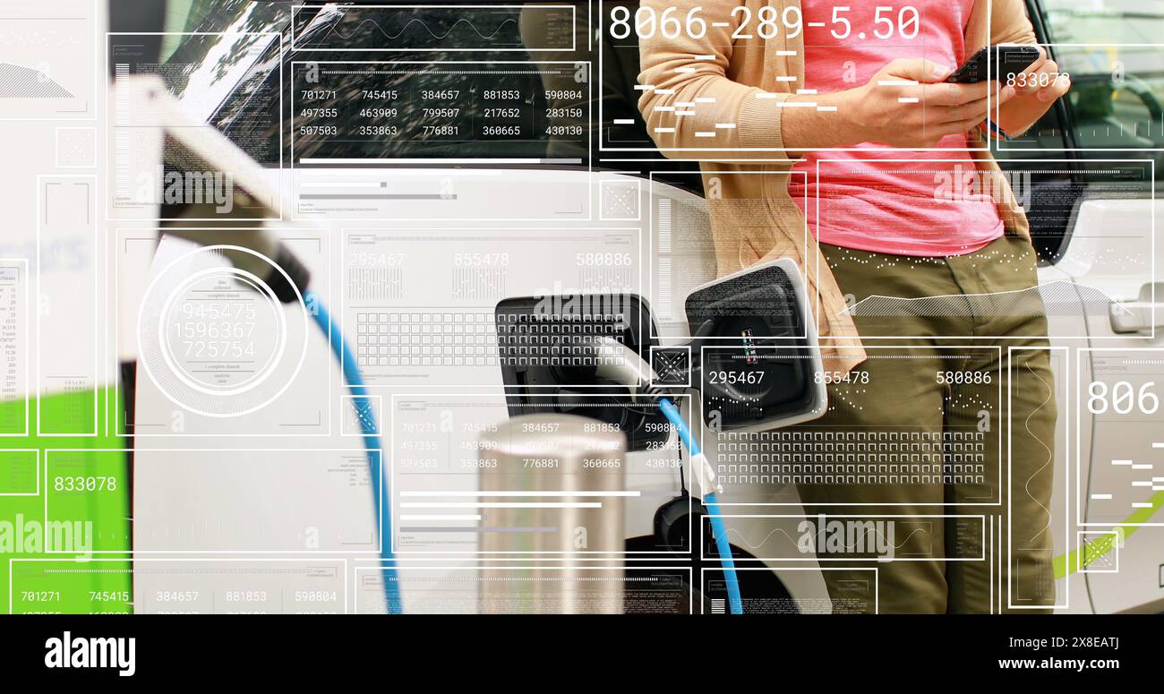 A man is using a mobile phone while charging an electric car at a ...
