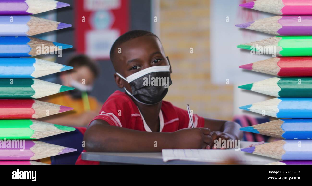 African American student wearing mask, writing with colorful pencils ...
