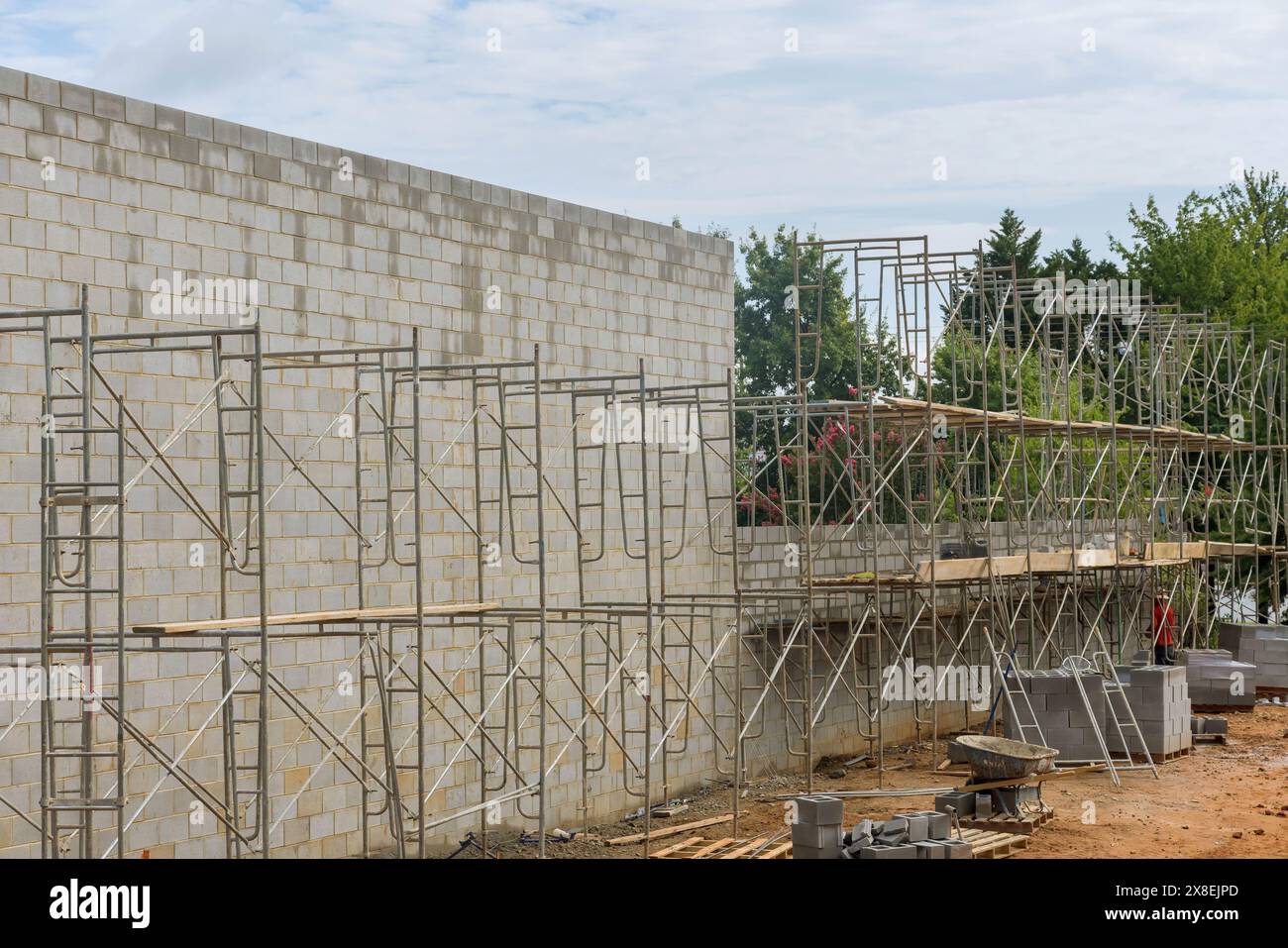 On scaffolding, bricklayer builds concrete wall from concrete blocks ...