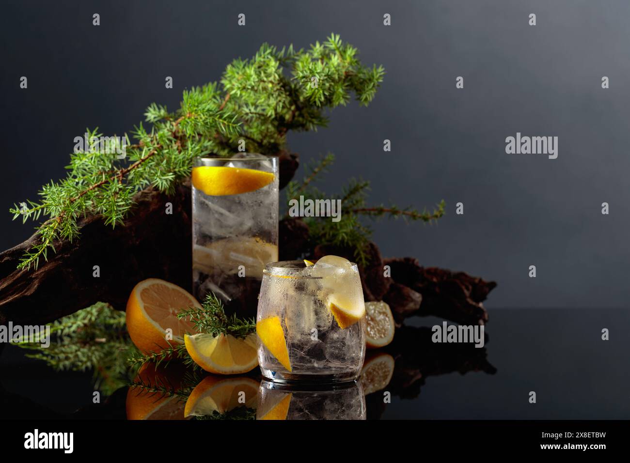 Cocktail gin-tonic with ice and lemon on a black reflective background ...