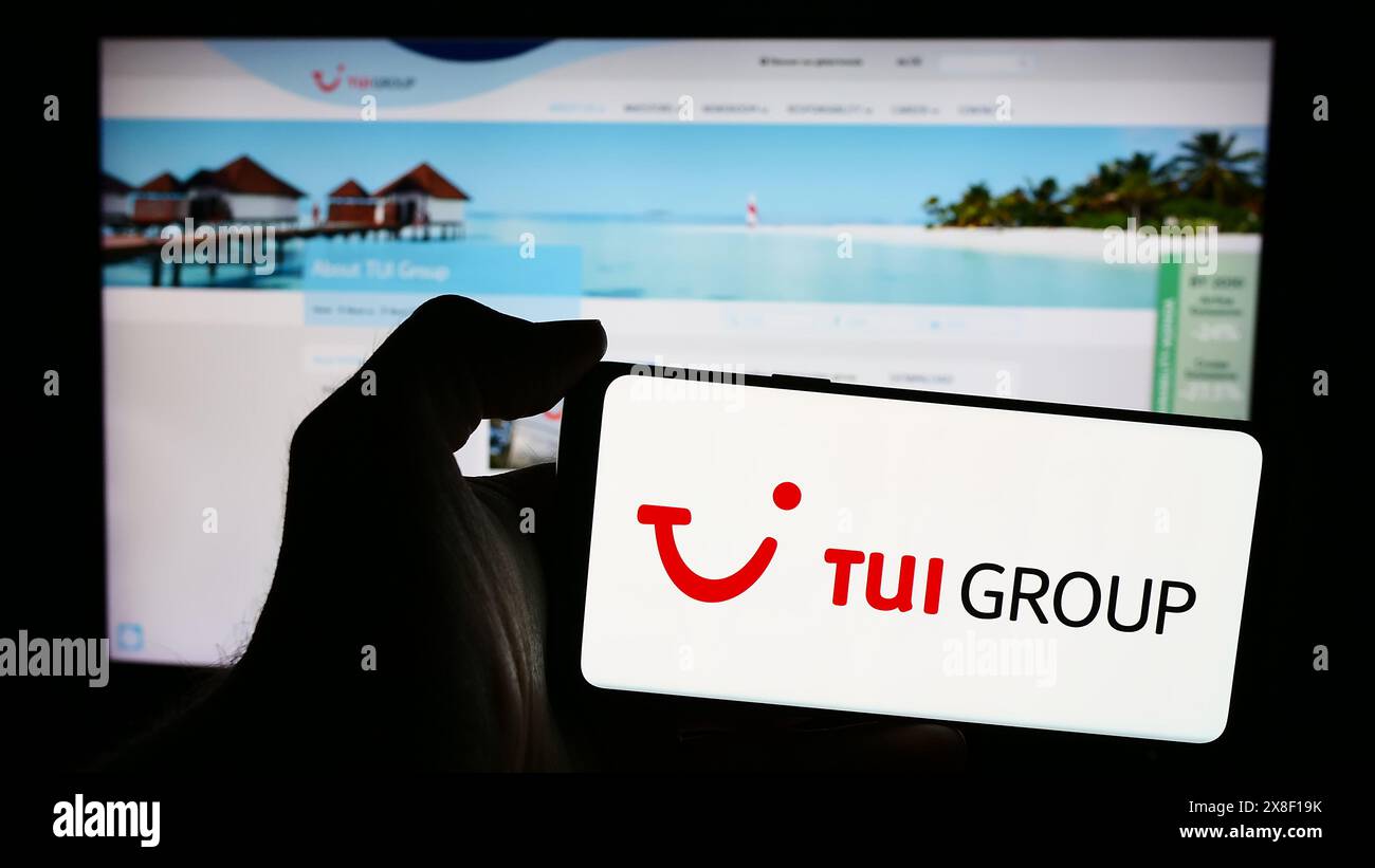 Person holding mobile phone with logo of German travel and tourism company TUI AG in front of ...