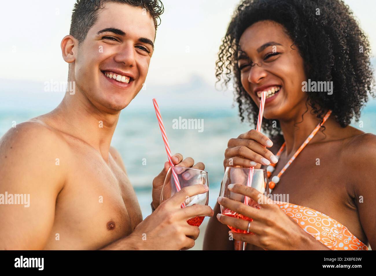 Happy couple enjoying refreshing drinks on the beach - smiling and laughing - summer fun and ...