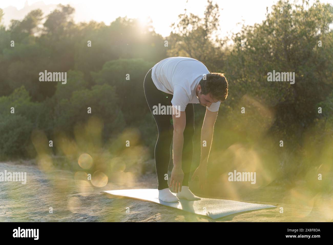 A young man performs body stretches in nature during sunset. Healthy ...