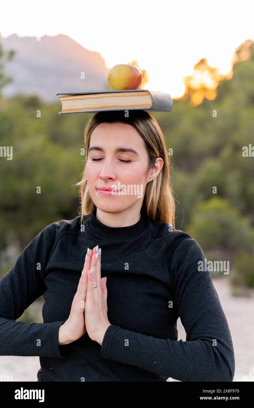 Woman meditating with a book and an apple on her head. Body and mind in ...
