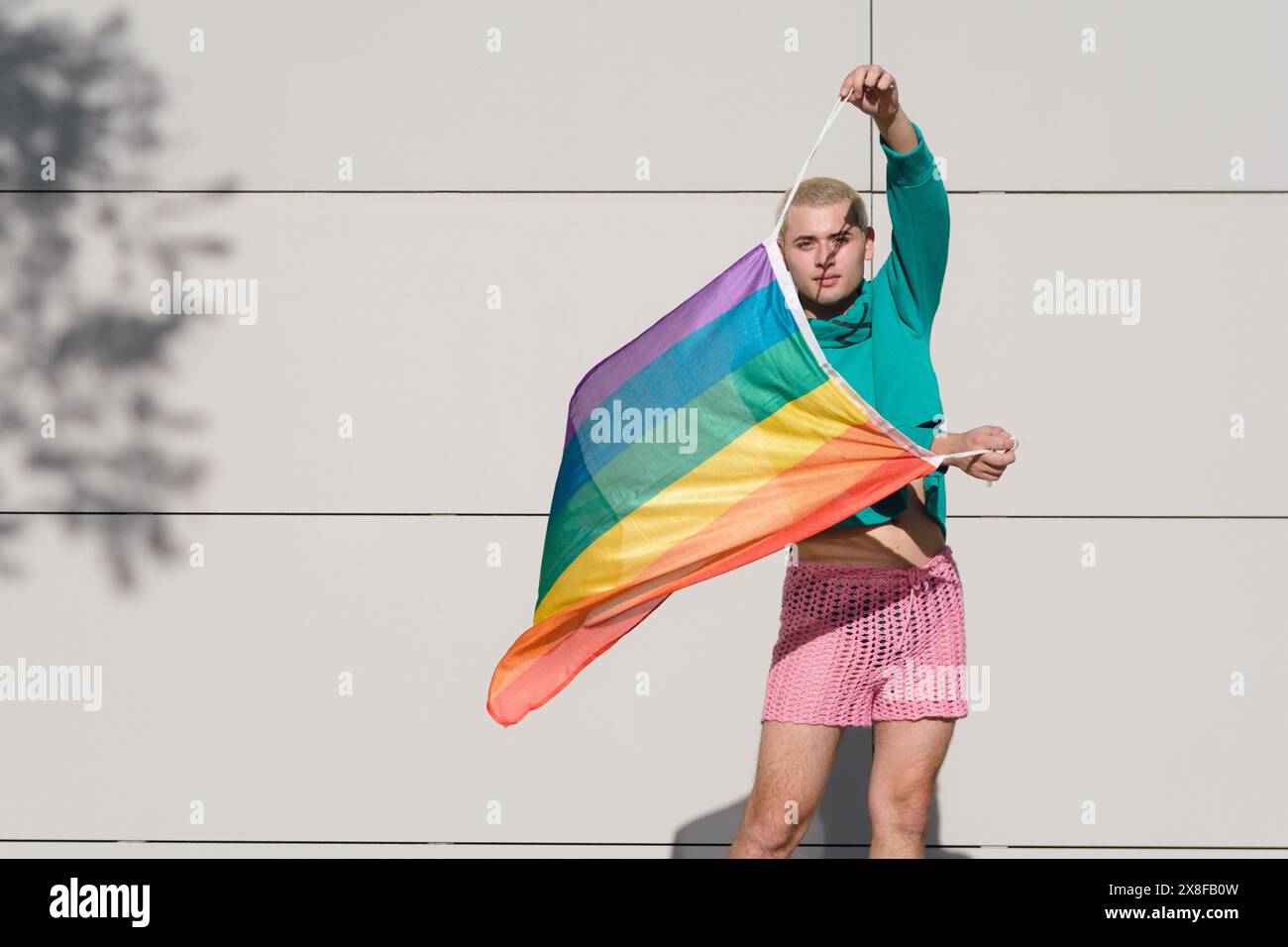 A Latin Young Man outdoors waving a rainbow flag. The man is wearing a ...