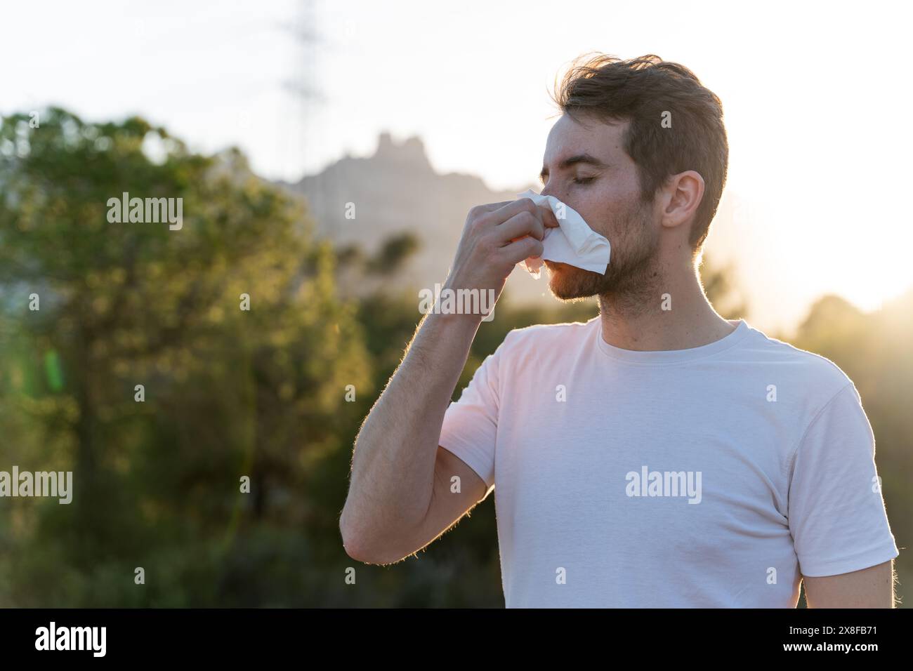 Sick man surrounded by nature blowing his nose and sneezing for pollen ...