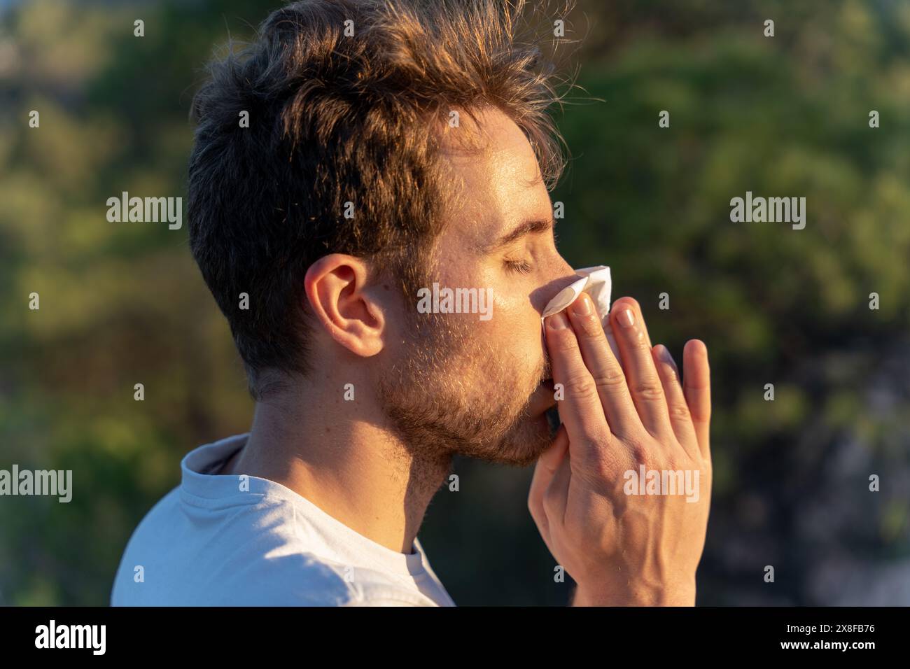 Sick man surrounded by nature blowing his nose and sneezing for pollen ...