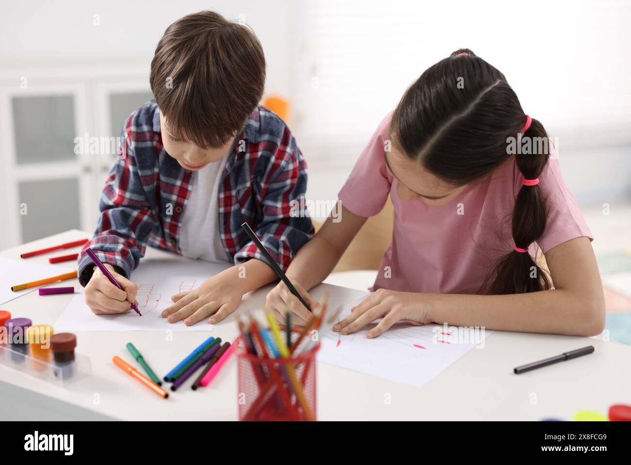 Happy brother and sister drawing at white table in room Stock Photo - Alamy