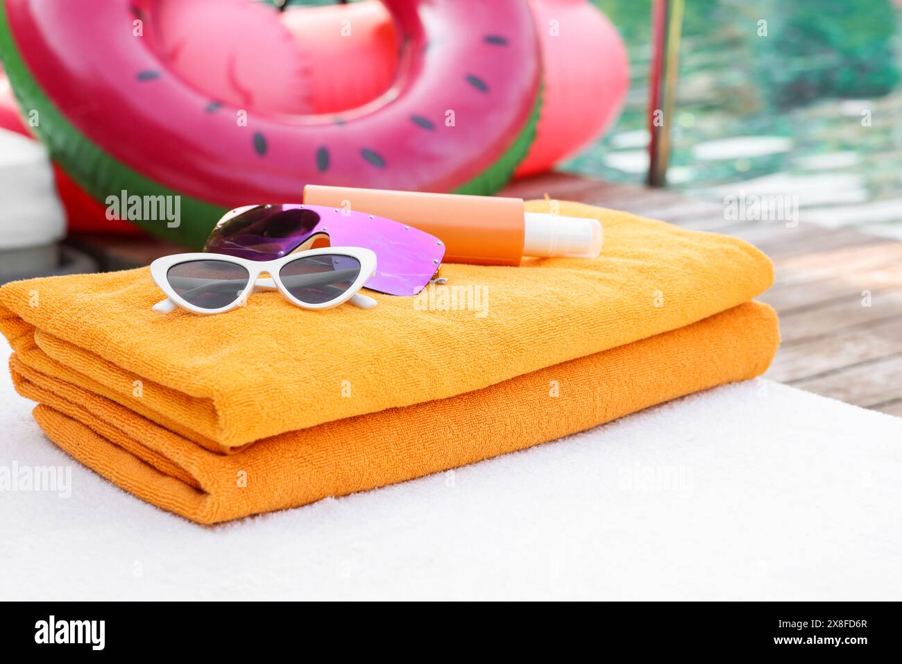 Beach towels, sunglasses and sunscreen on sunbed near outdoor swimming ...