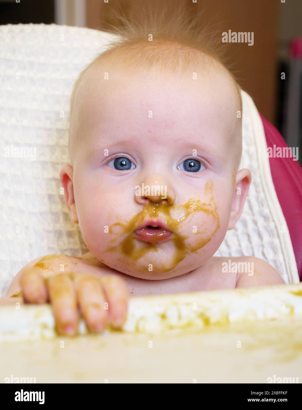 A cute baby with blue eyes has broccoli puree smeared all over their ...