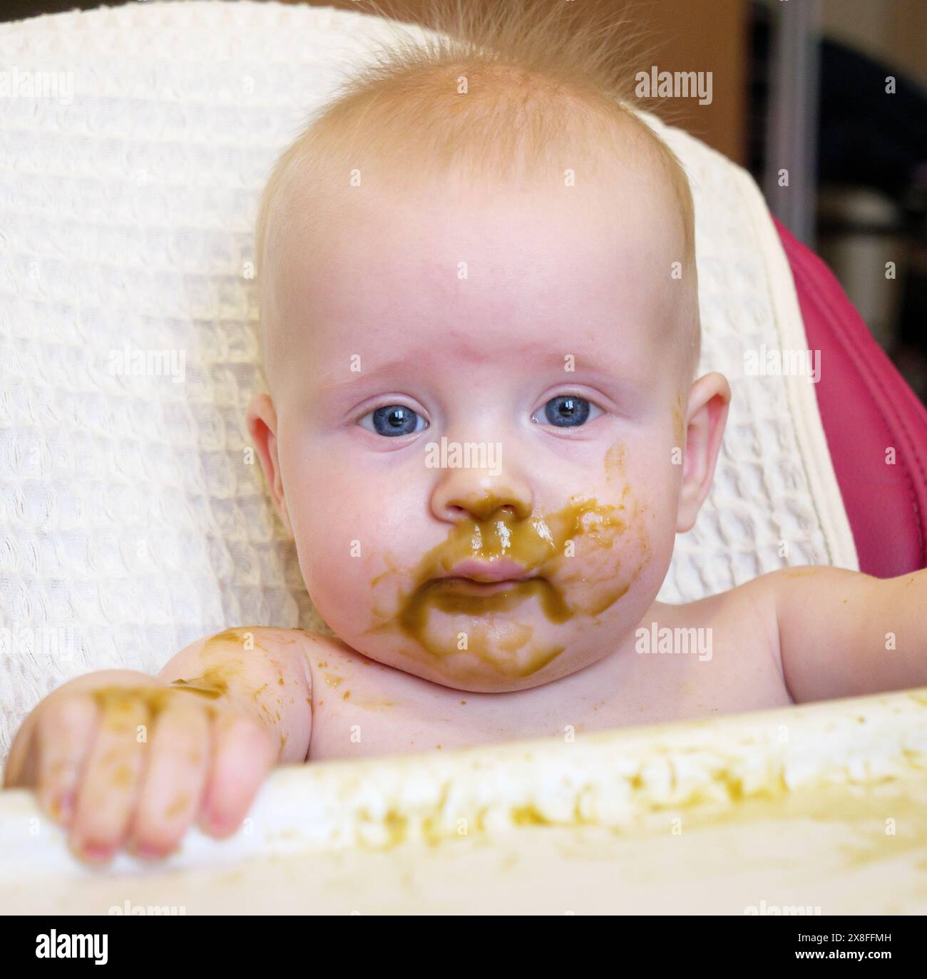 A cute baby with blue eyes has broccoli puree smeared all over their ...