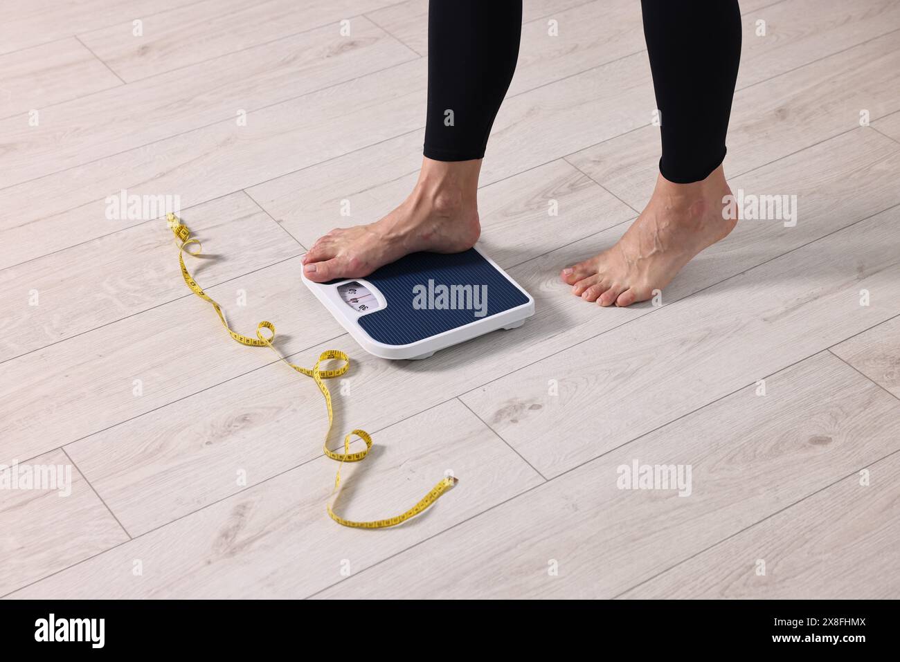 Woman stepping on floor scale and measuring tape at home, closeup ...