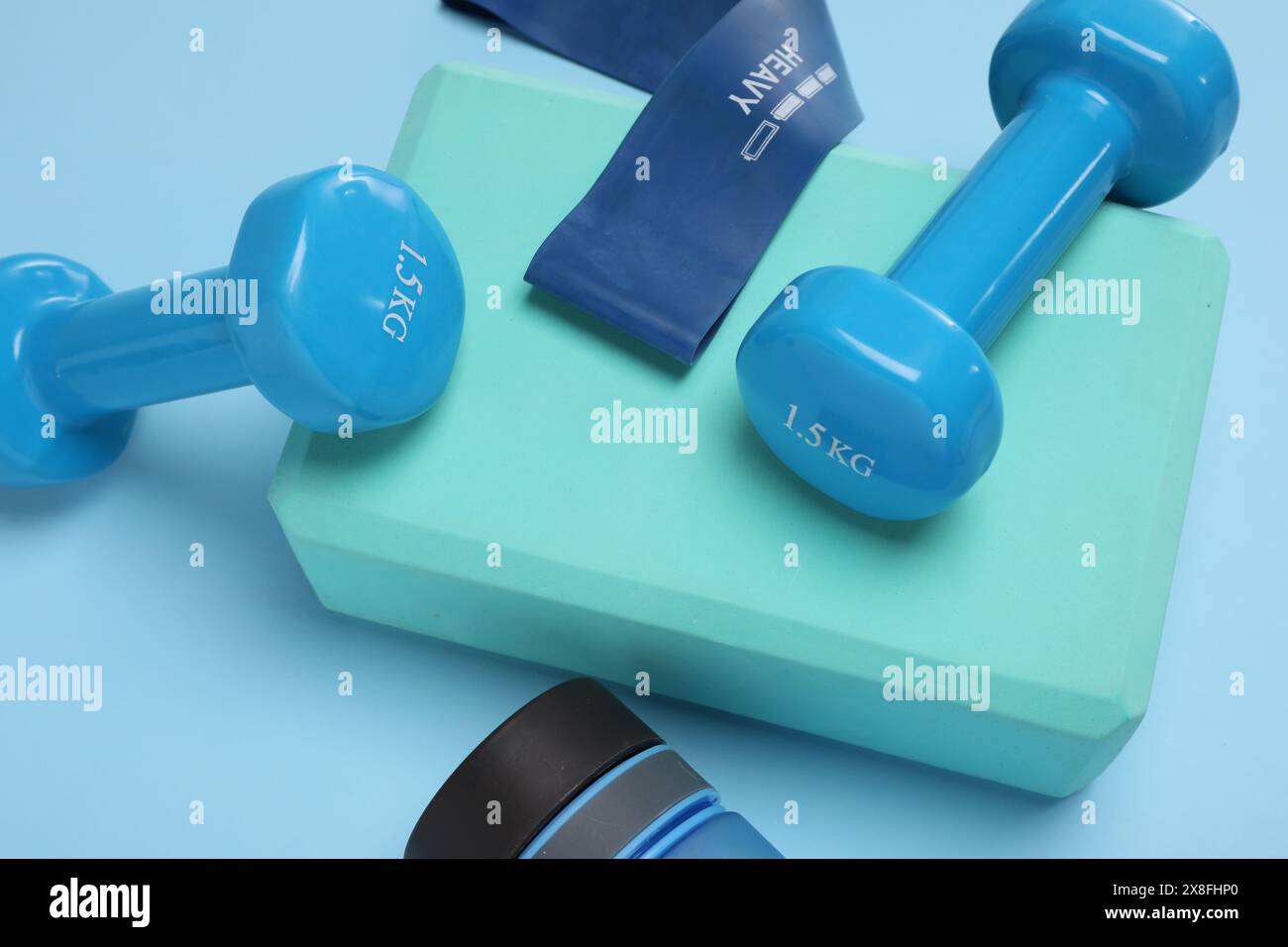 Two dumbbells, yoga block, fitness elastic band and bottle on light ...