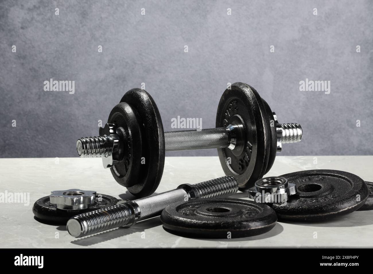 Barbell and parts of one on light table against grey background Stock ...
