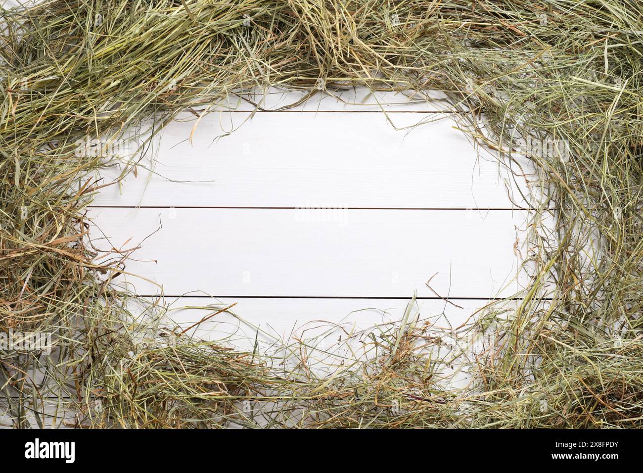 Frame made of dried hay on white wooden table, top view. Space for text ...