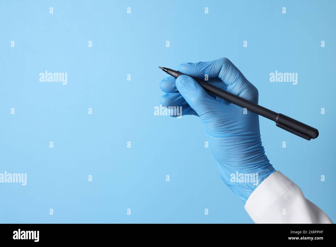 Doctor wearing medical glove writing something on light blue background ...