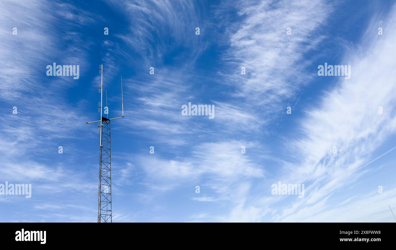 A tall communication tower stands against a clear blue sky filled with wispy clouds Stock Photo ...
