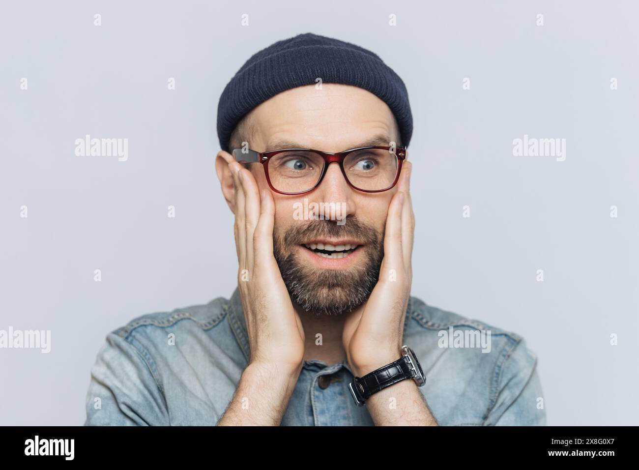 Surprised man with hands on cheek standing before a pale background ...