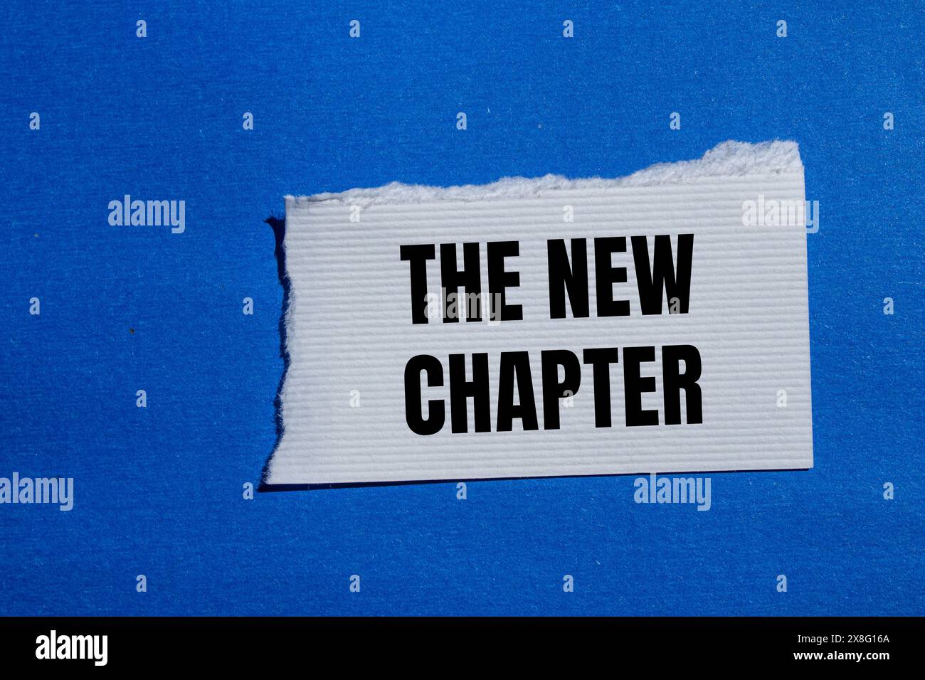 The new chapter words written on ripped white paper piece with blue ...