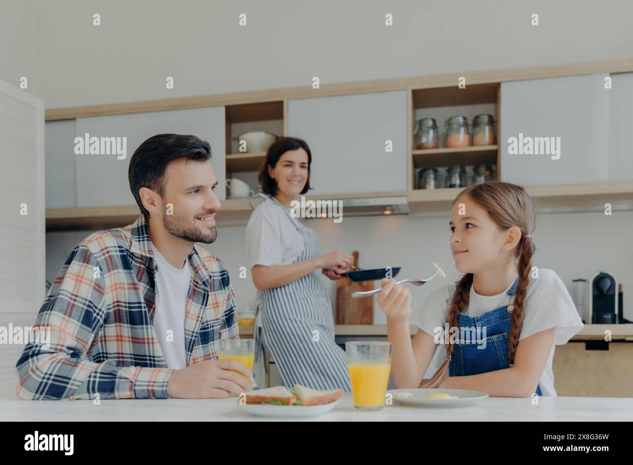 Candid breakfast scene with father and daughter talking while mom flips ...