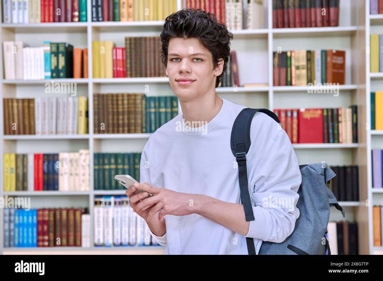 Teenage male student with backpack using smartphone, inside college ...