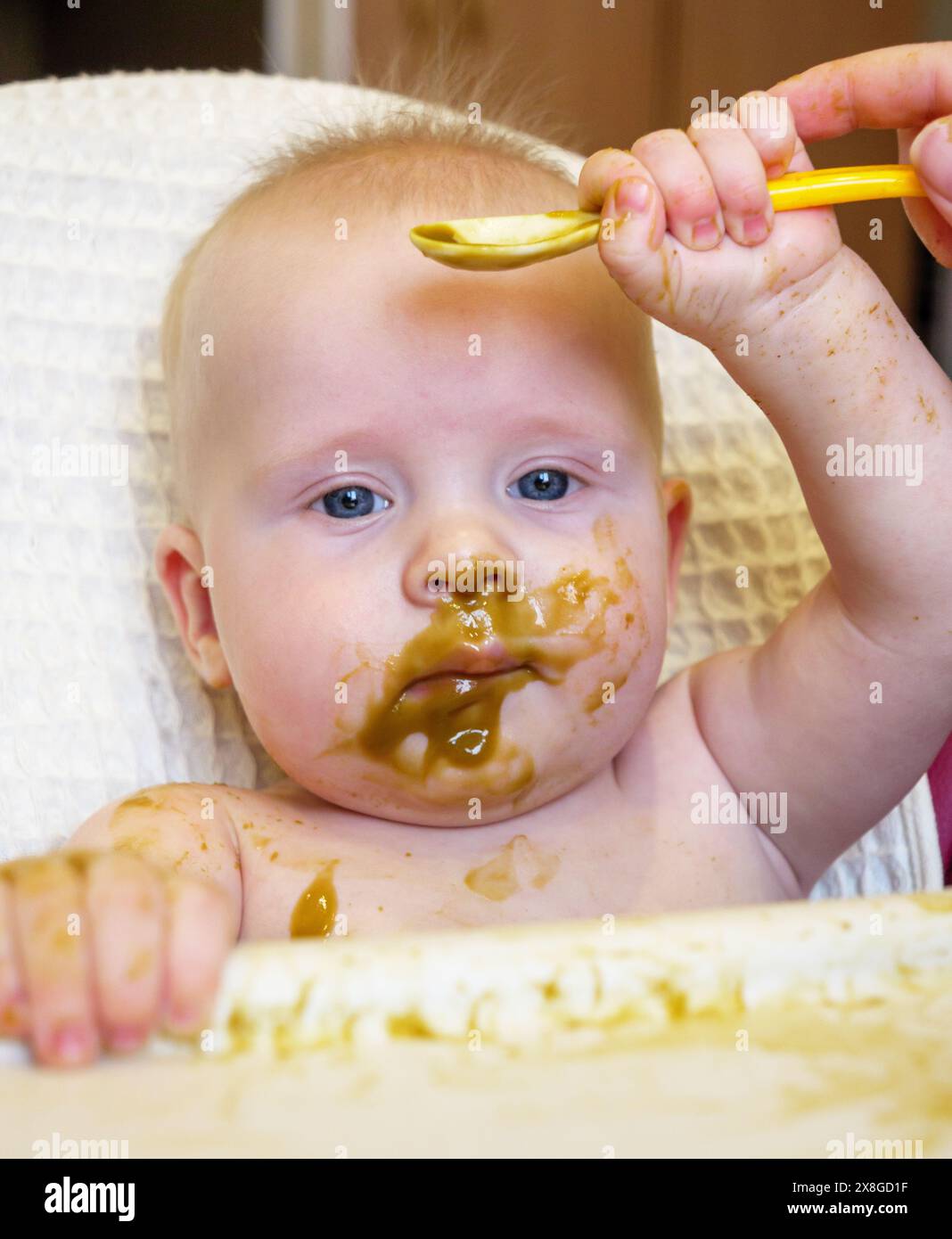 A cute baby with blue eyes has broccoli puree smeared all over their ...