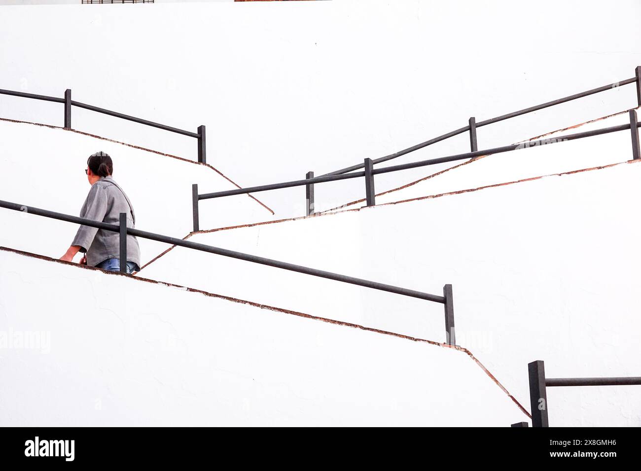 A pedestrian walks up a steep walkway against a pattern of black lines ...