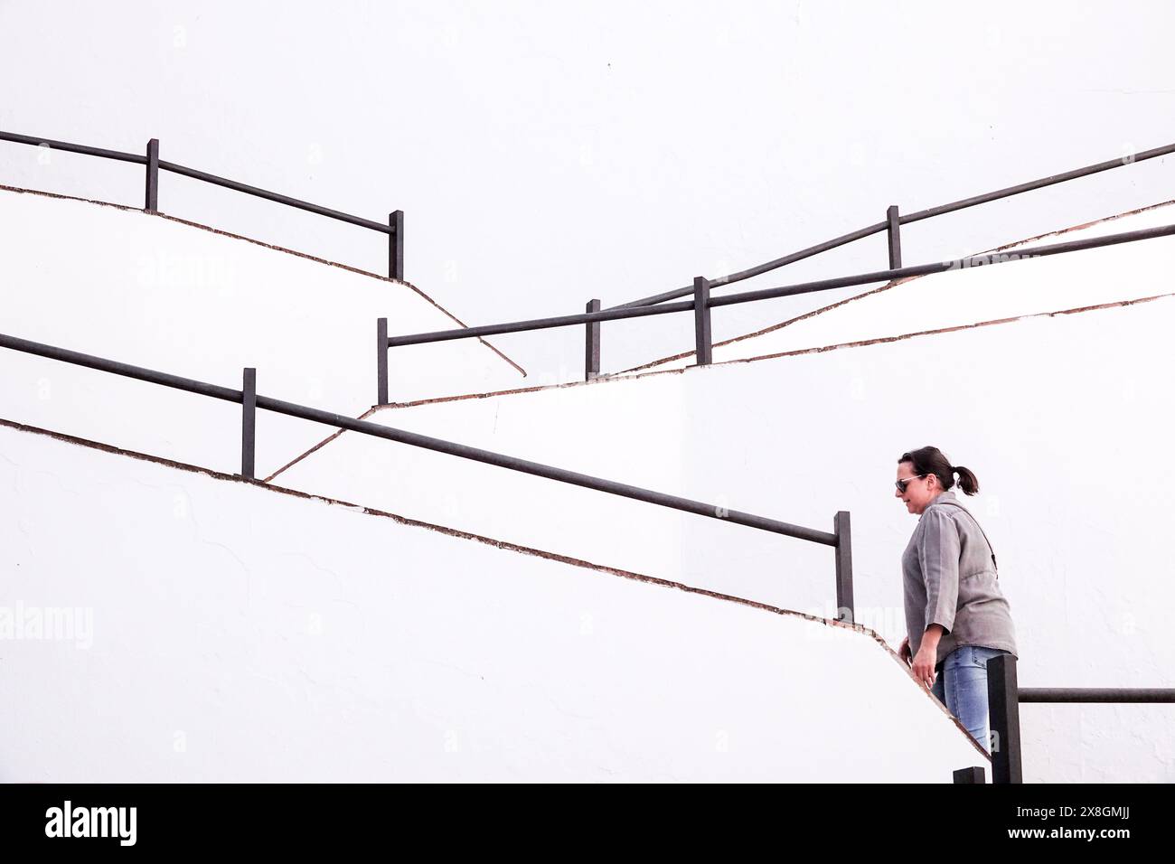 A pedestrian walks up a steep walkway against a pattern of black lines ...