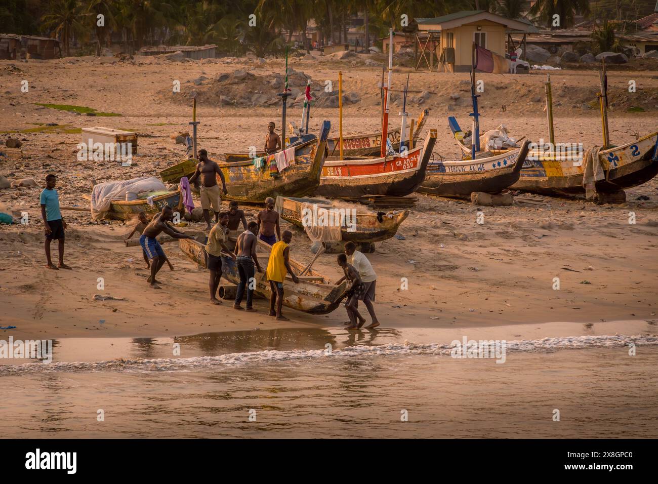 The group of fishermen and the fishing boat (piroga) on the sandy beach ...