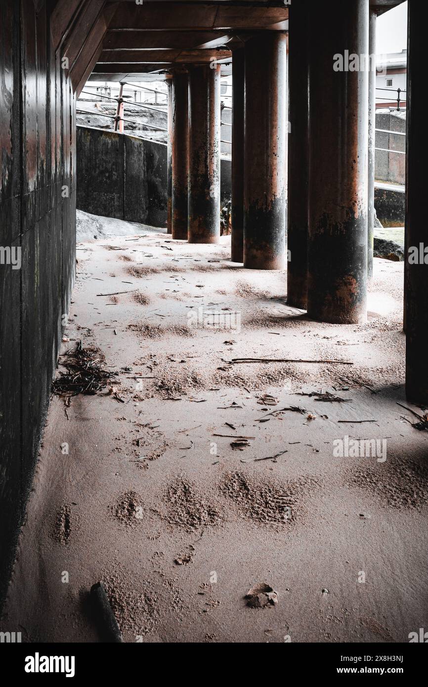 Serene walkway under urban bridge with concrete pillars and sandy floor ...
