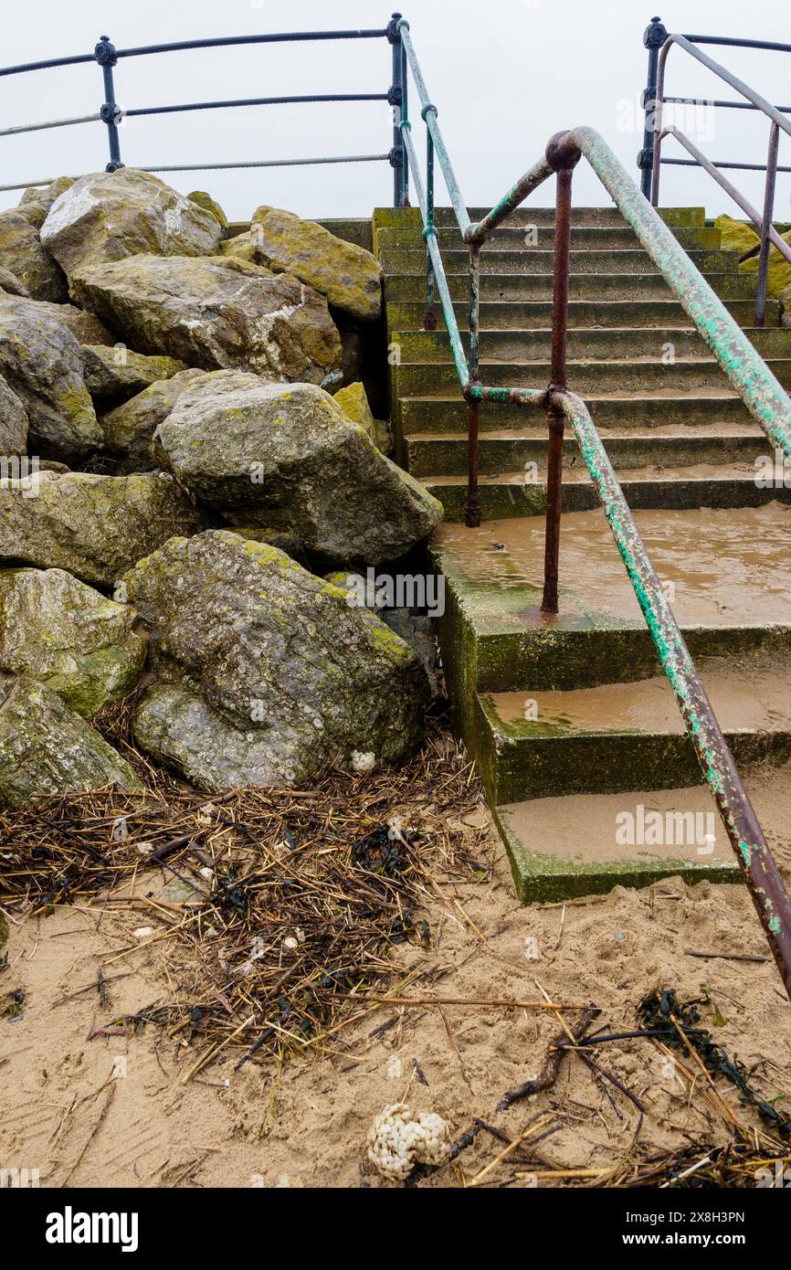 Weathered stone steps from sand-covered beach, bordered by mossy rocks ...