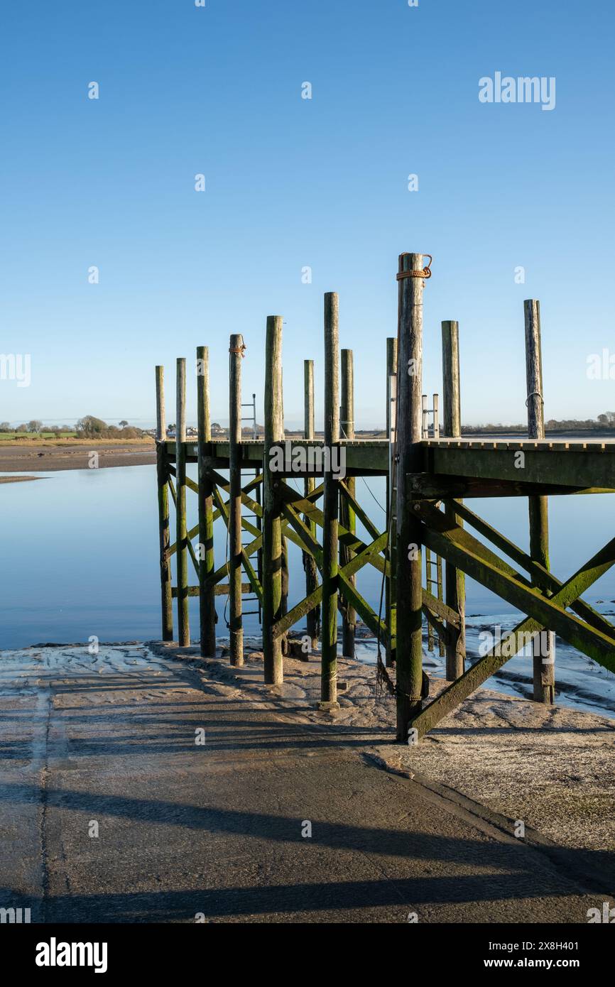 A weathered wooden pier over calm, reflective water under a clear blue ...