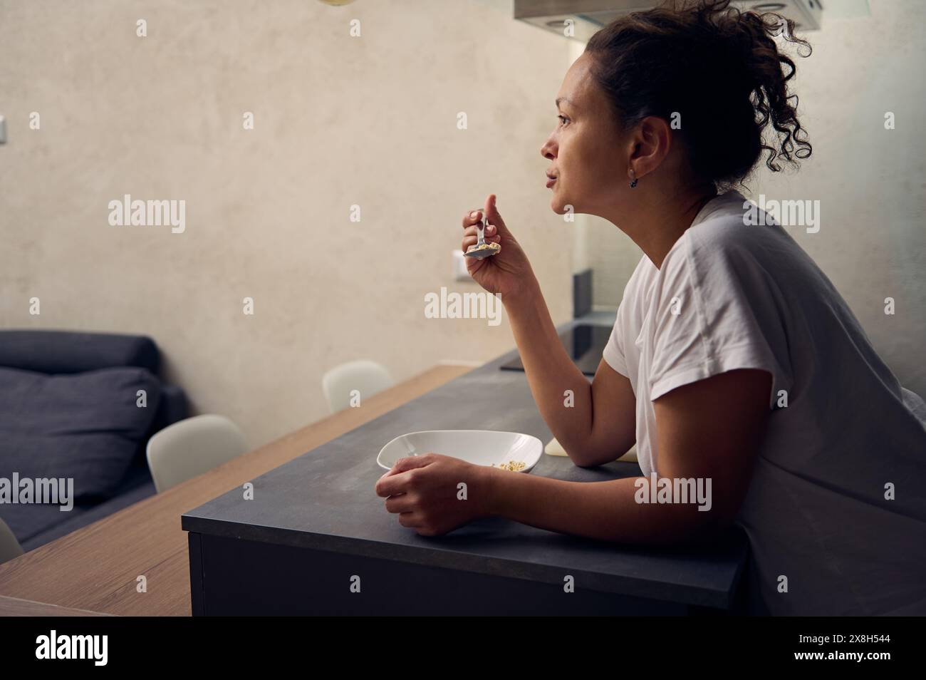 Side portrait of a curly haired multi ethnic woman eating oat flakes ...