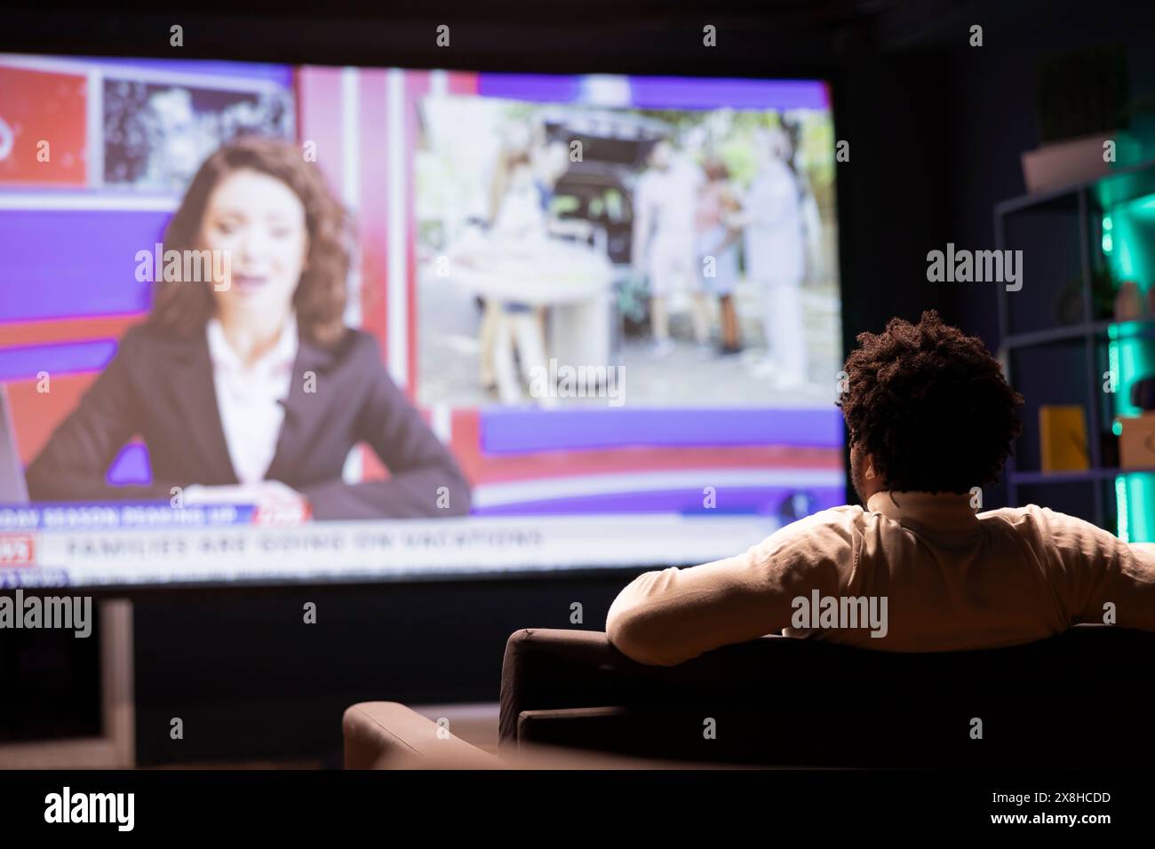 Man sitting on couch in front of ultrawide smart TV displaying news program broadcasting. Person ...
