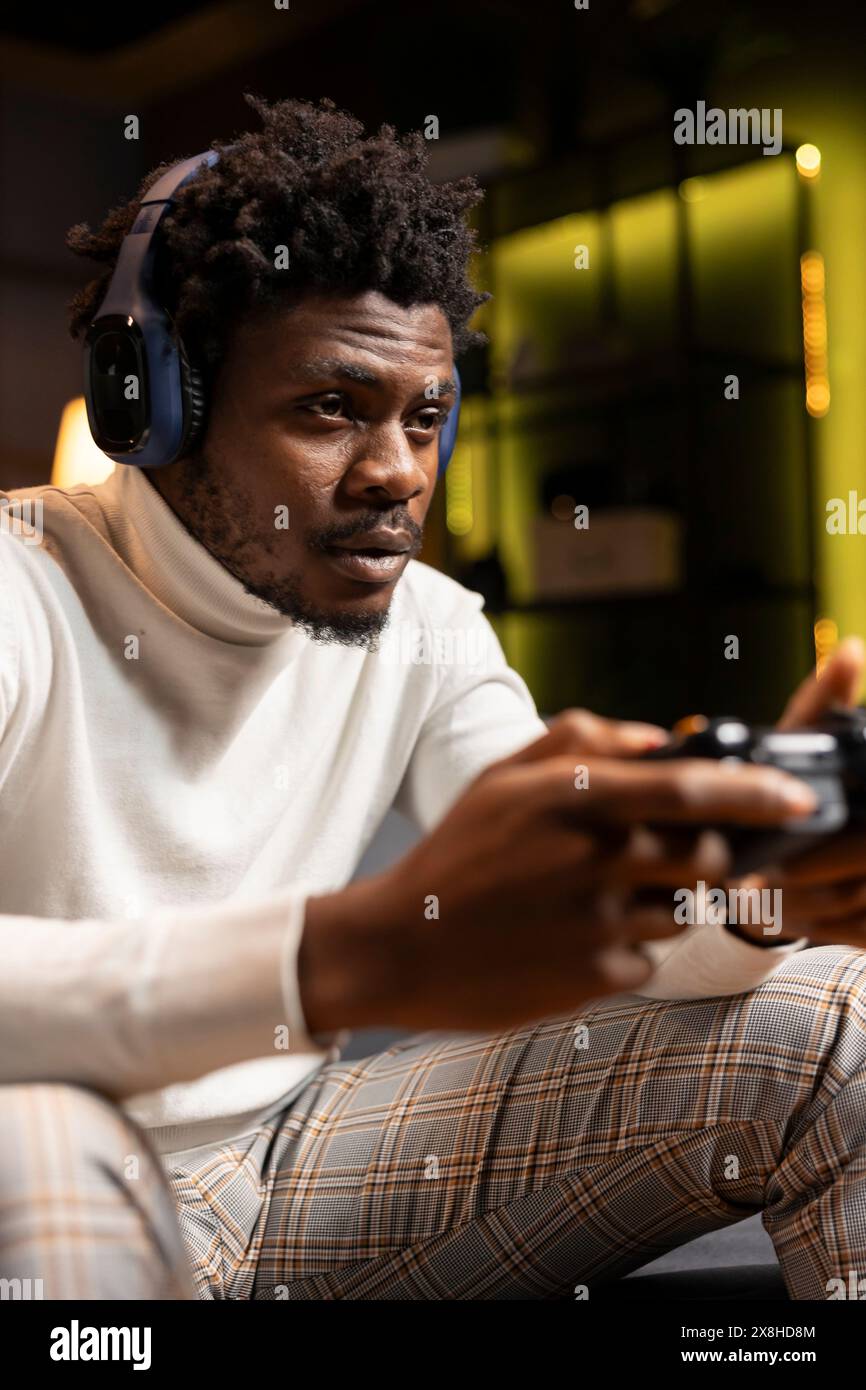 African american man playing videogame in yellow neon lit apartment ...