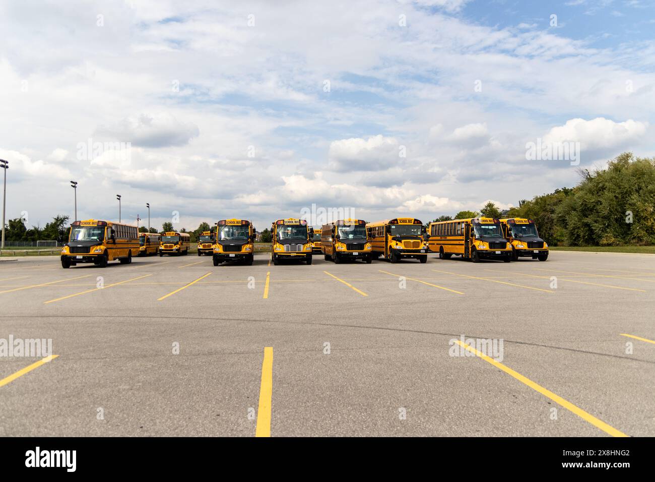 Yellow school buses lined up in an empty parking lot - under a partly ...
