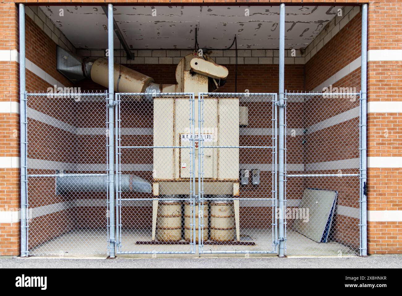 Beige machinery enclosed by chain-link fence - set against red brick ...